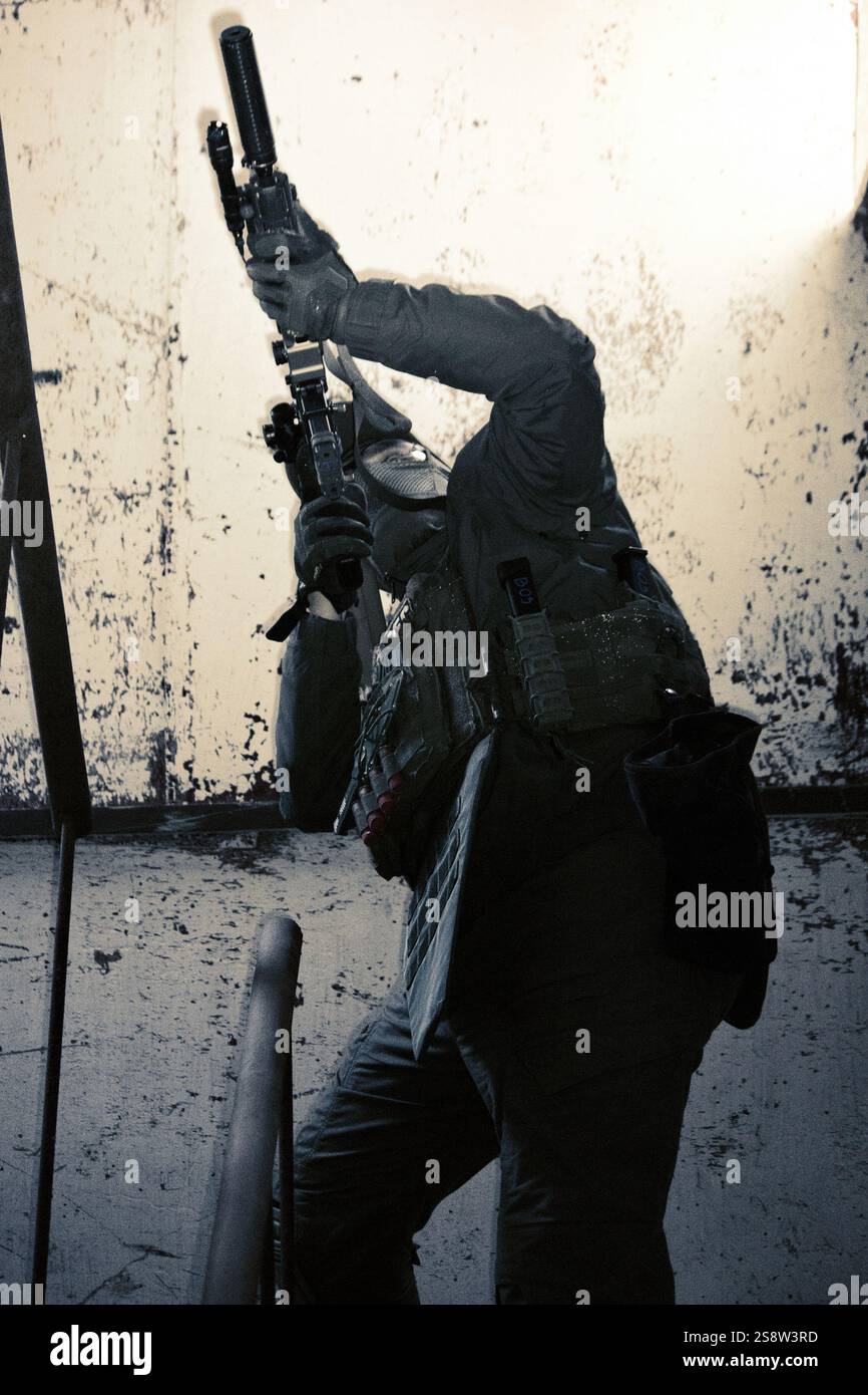 A tactical operator in military gear ascends a staircase in a dimly lit ...