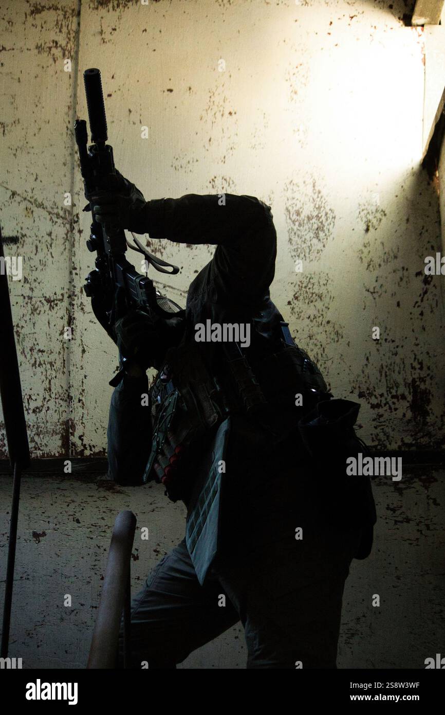 A tactical operator in military gear ascends a staircase in a dimly lit ...