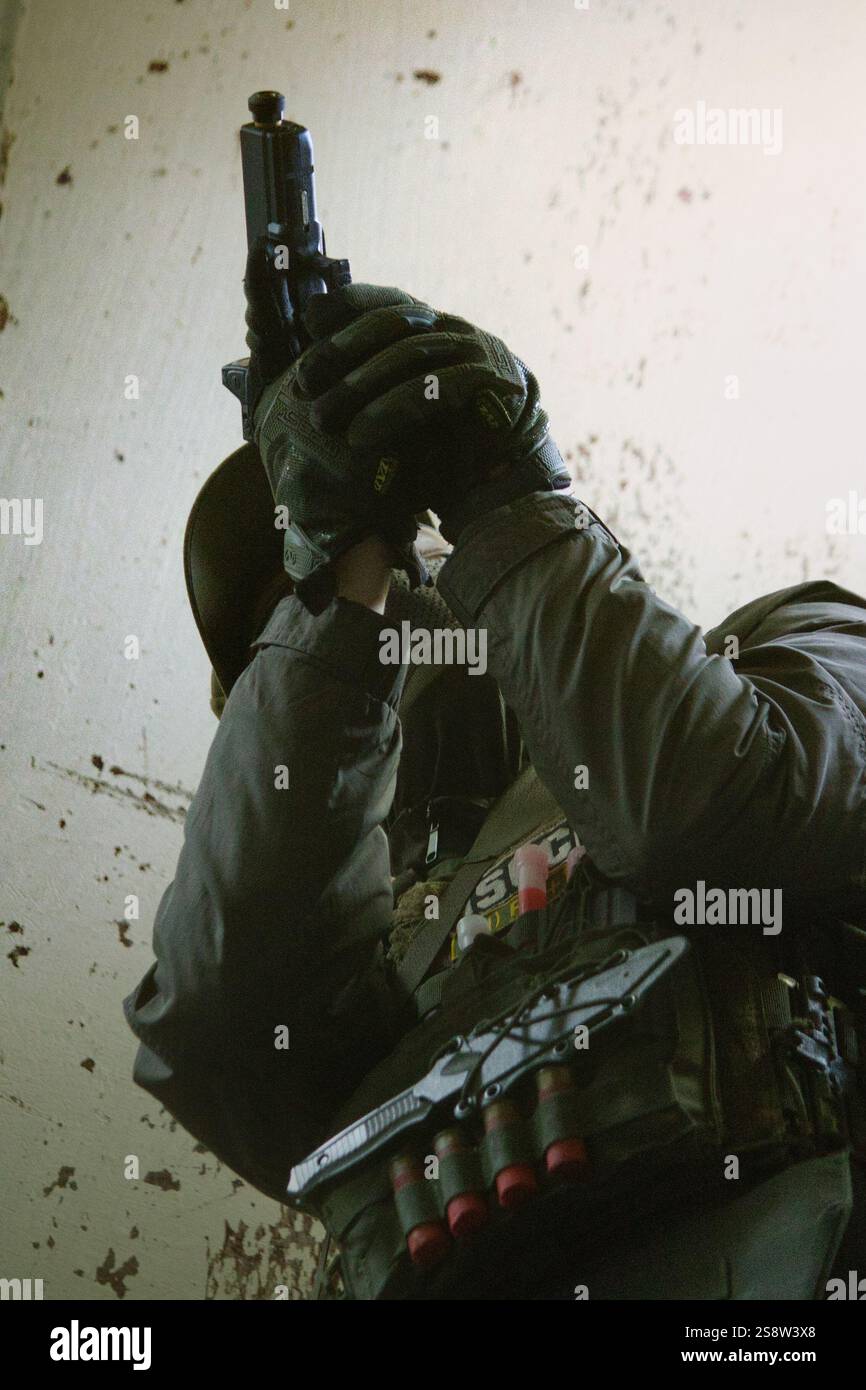 A tactical operator in military gear ascends a staircase in a dimly lit ...