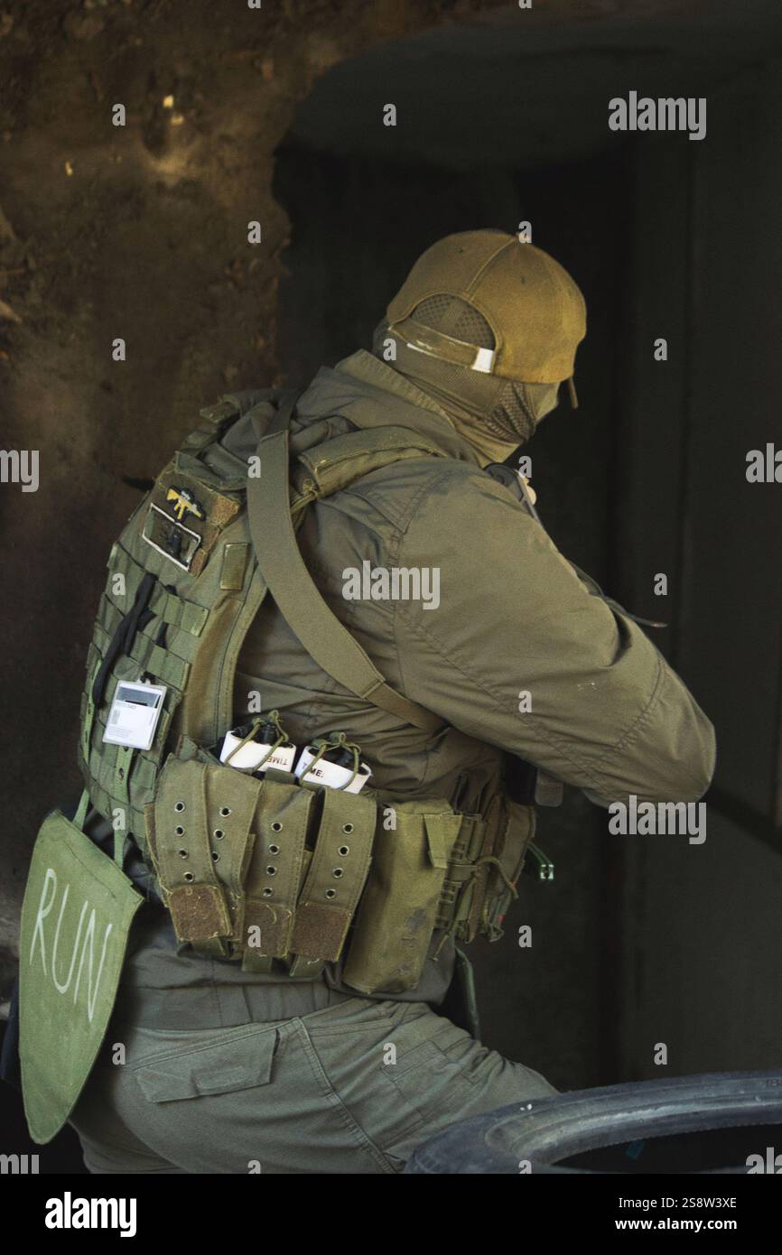 A tactical operator dressed in military gear and a cap stands inside an ...
