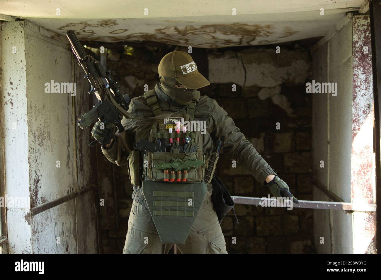 A tactical operator dressed in military gear and a cap stands inside an ...
