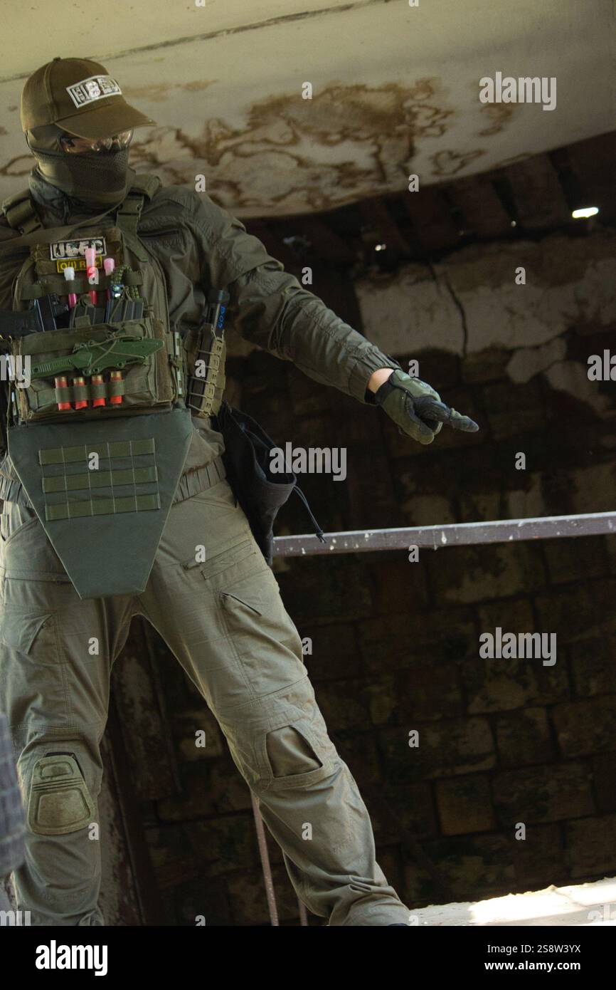 A tactical operator dressed in military gear and a cap stands inside an ...