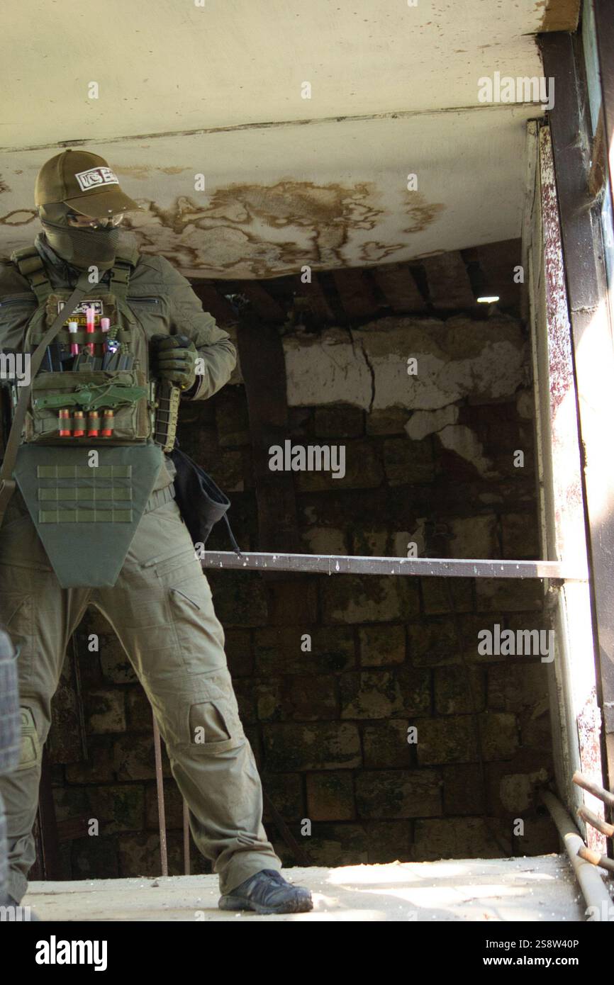 A tactical operator dressed in military gear and a cap stands inside an ...