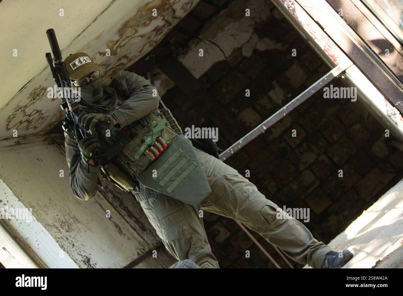 A tactical operator dressed in military gear and a cap stands inside an ...