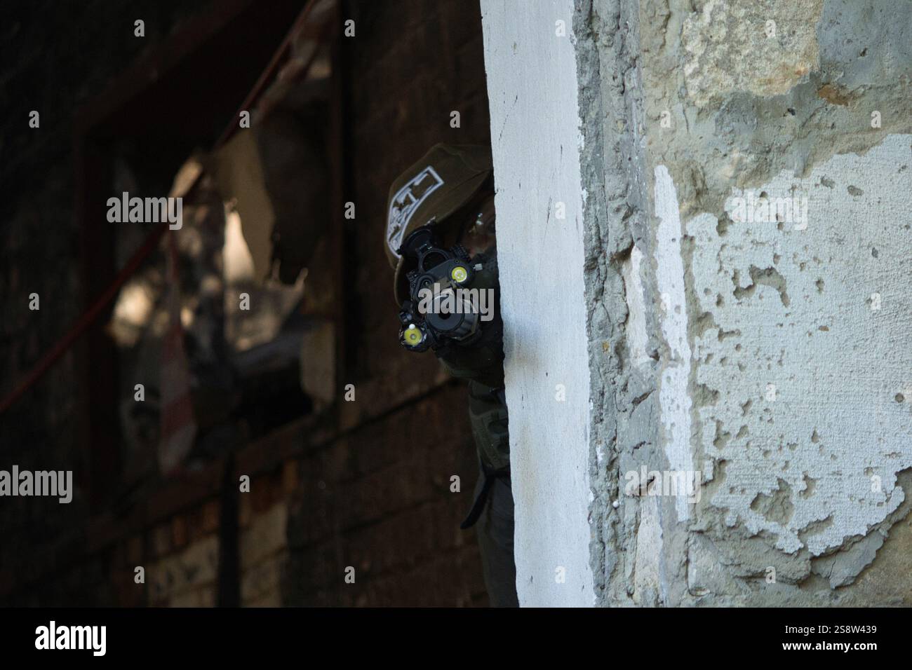 A tactical operator in military gear takes cover behind a moss-covered ...