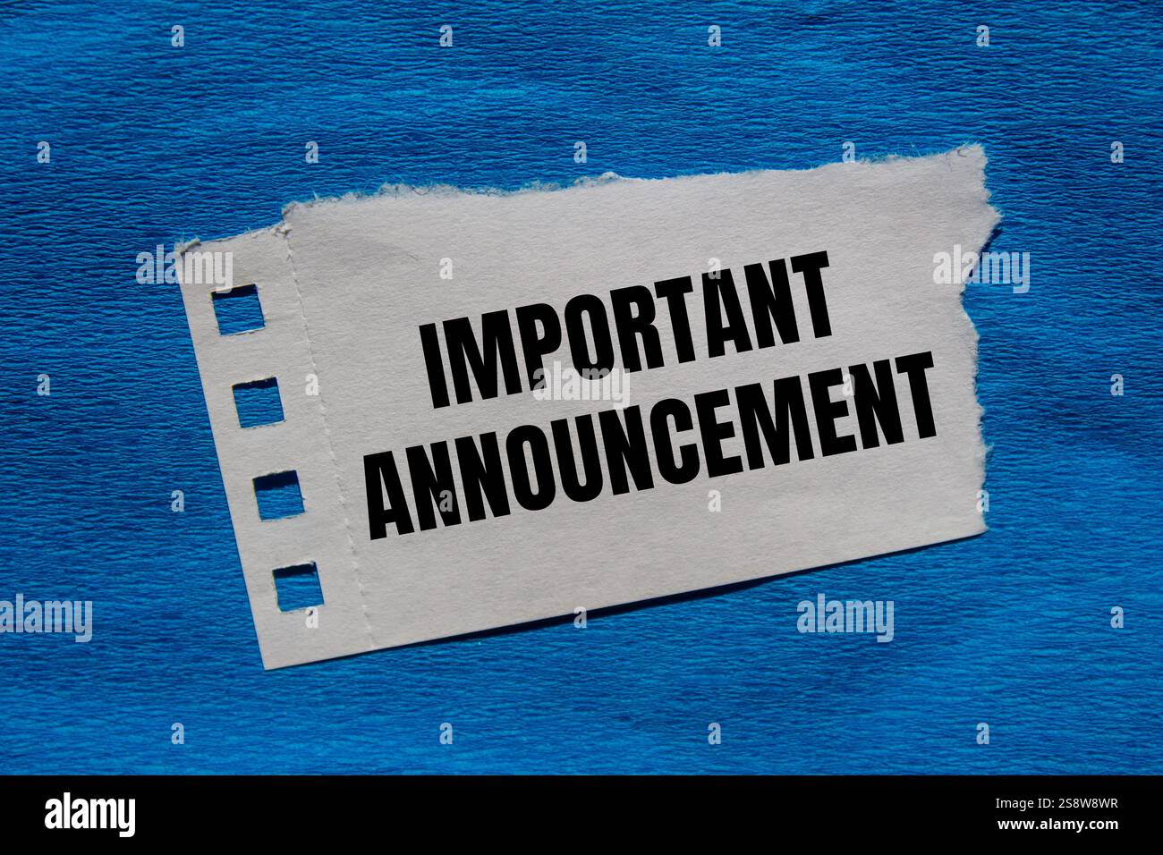 Important announcement message written on ripped torn paper piece with blue background ...