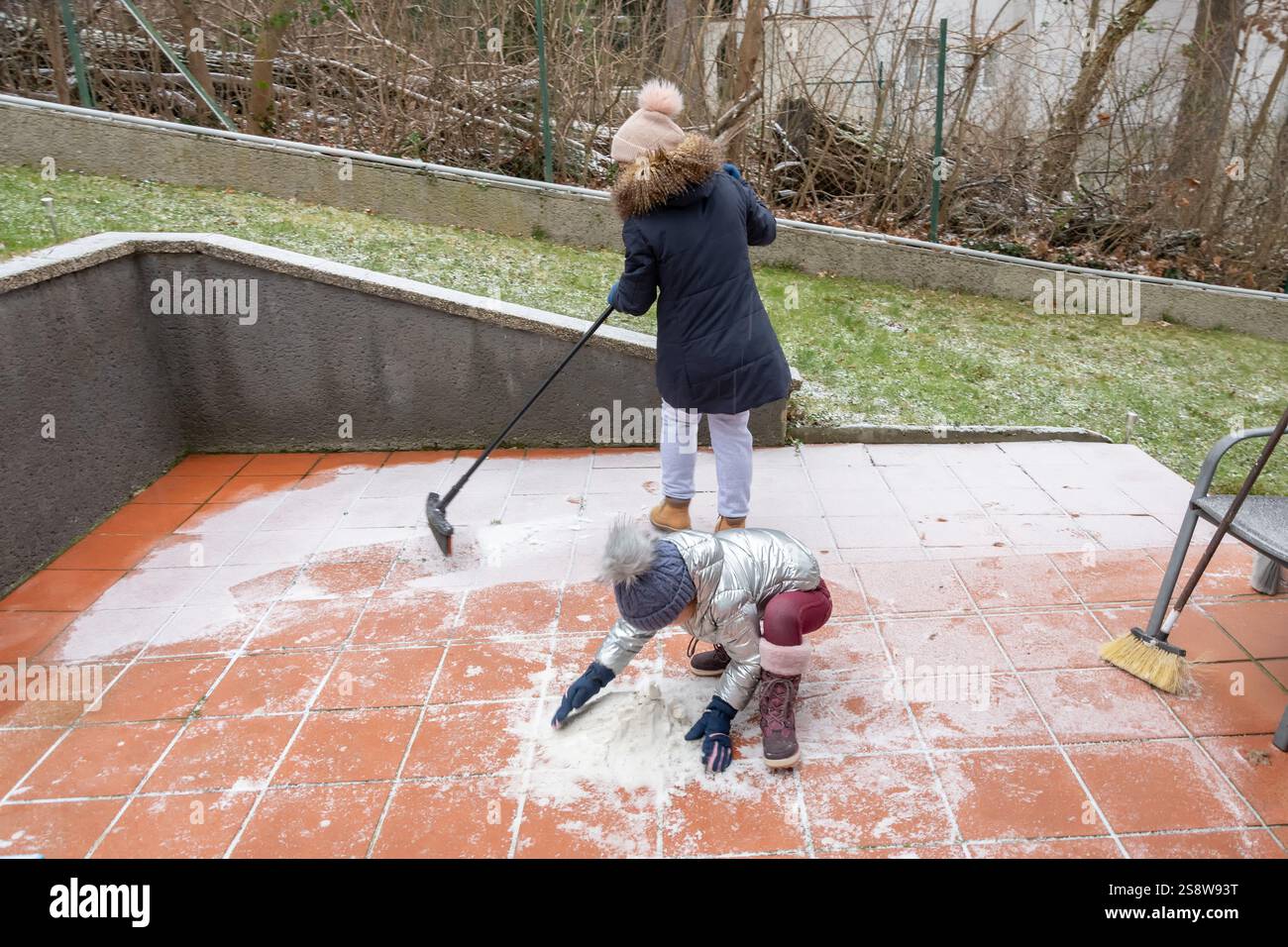 Family worries: mum teaches her child to brush the snow Stock Photo - Alamy