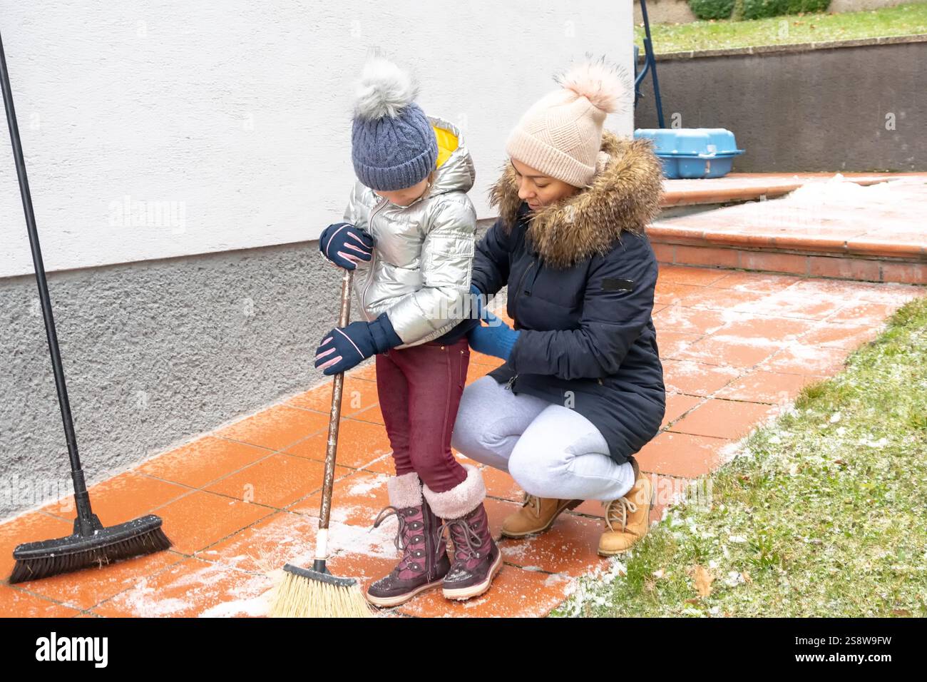 Cosy winter moment: mum fixing her daughter's clothes while shovelling ...