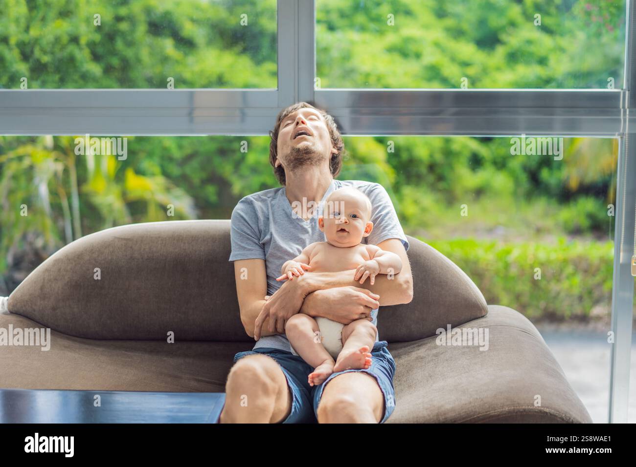 An exhausted father falls asleep on the couch while holding his 3-month ...