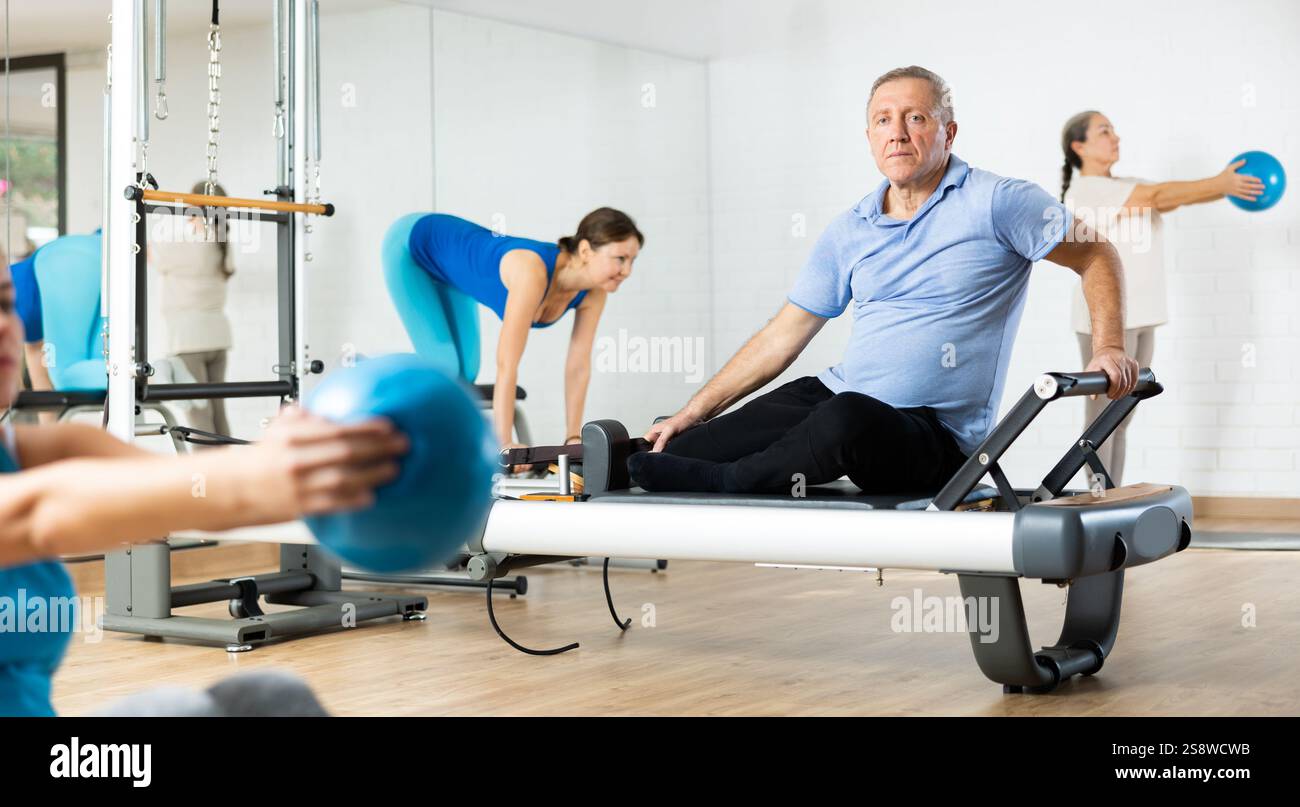 Elderly man performing exercises on reformer in pilates studio Stock ...