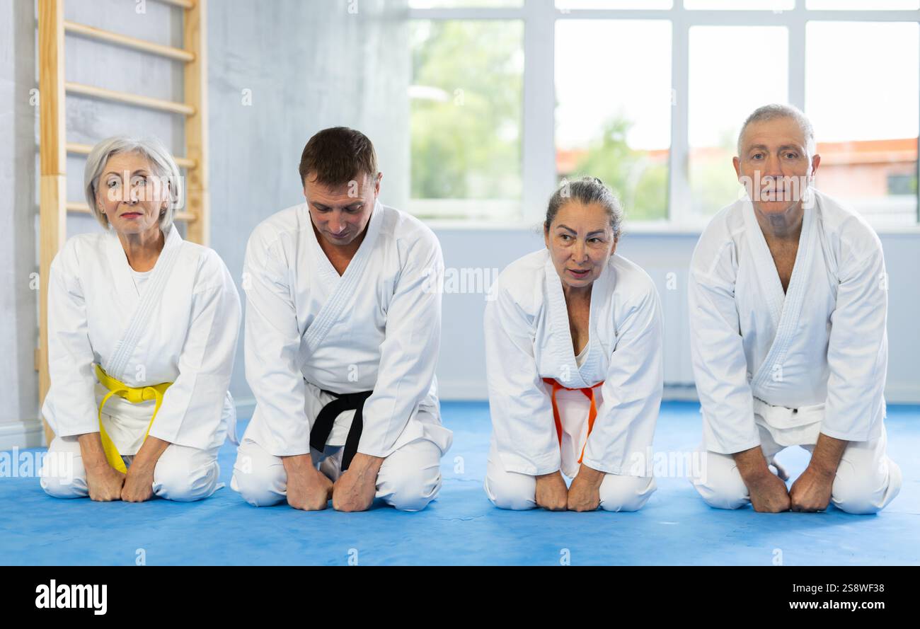 Mature judo practitioners in kimono sitting in seiza pose in sports ...