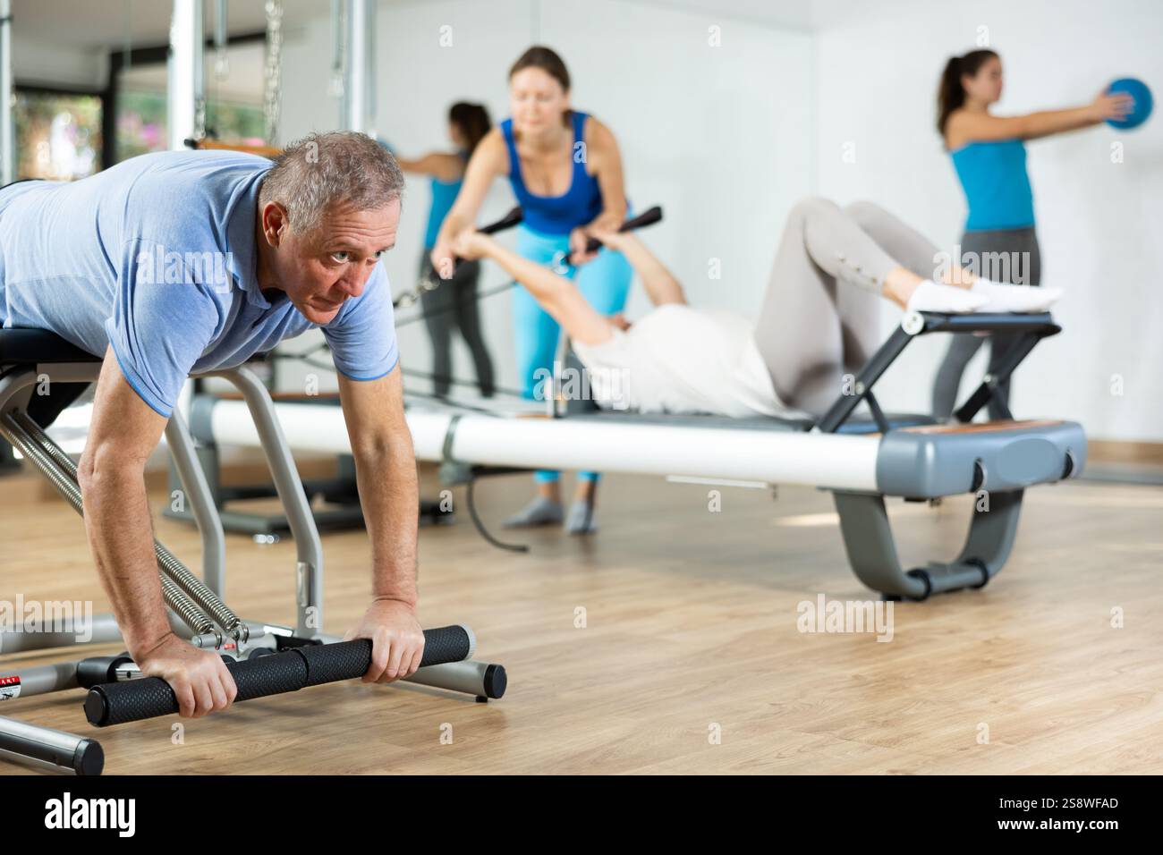 Aged man practicing pilates on pedal fitness chair in sports hall Stock ...