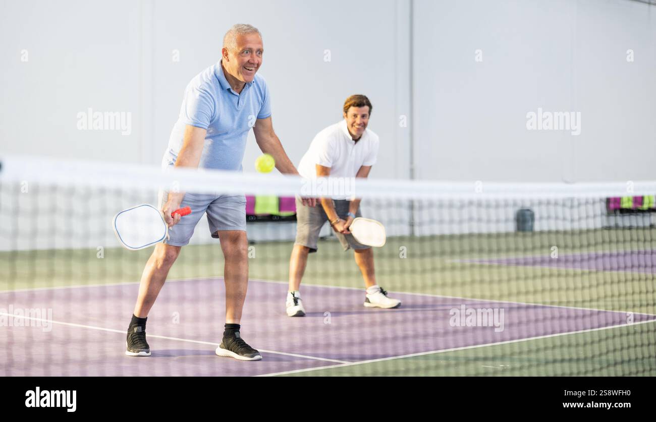 Elderly man playing pickleball in team with male partner indoors Stock ...