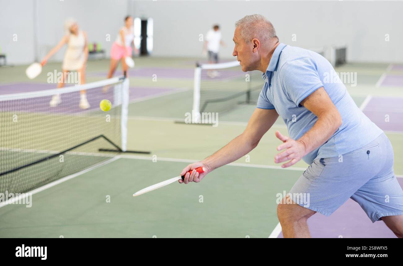 Aged man playing friendly pickleball match on indoor court Stock Photo ...