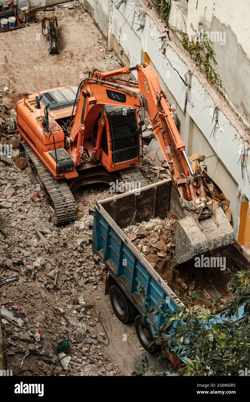 Excavator removing debris from a demolition site and dumping it into ...
