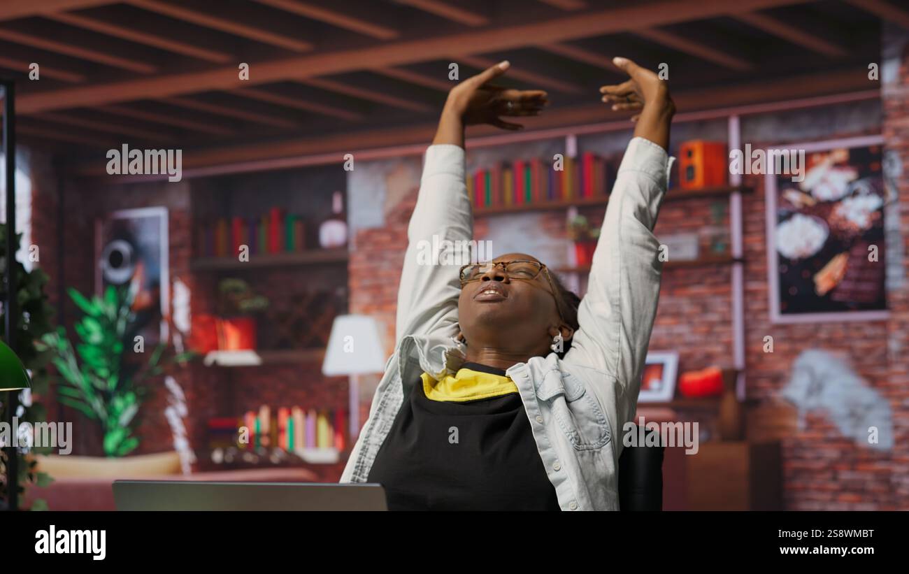 Woman in home office stretches back, feeling fatigued while working on ...