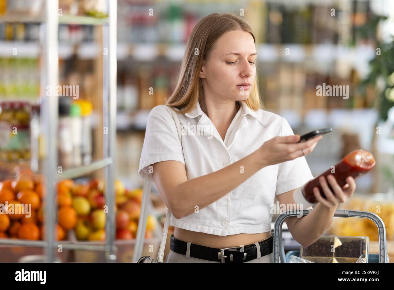 Female shopper scanning QR code on bottle ketchup label in grocery ...