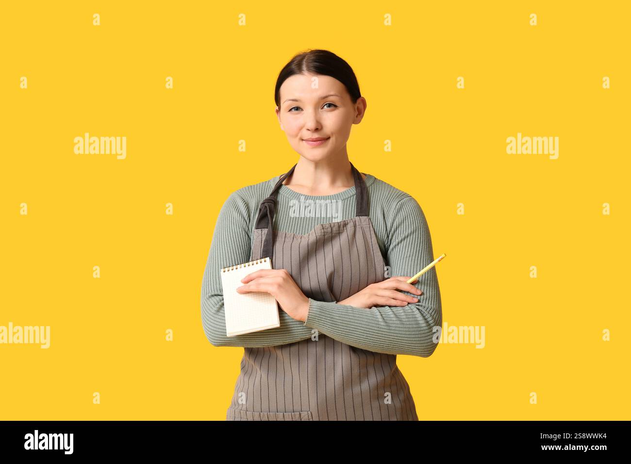 Beautiful young waitress with notebook and crossed arms on yellow ...