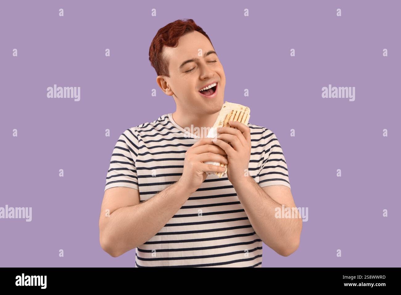 Young man eating doner kebab on purple background Stock Photo - Alamy