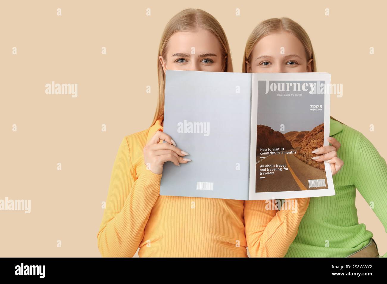 Beautiful young sisters hiding behind open magazine on beige background ...