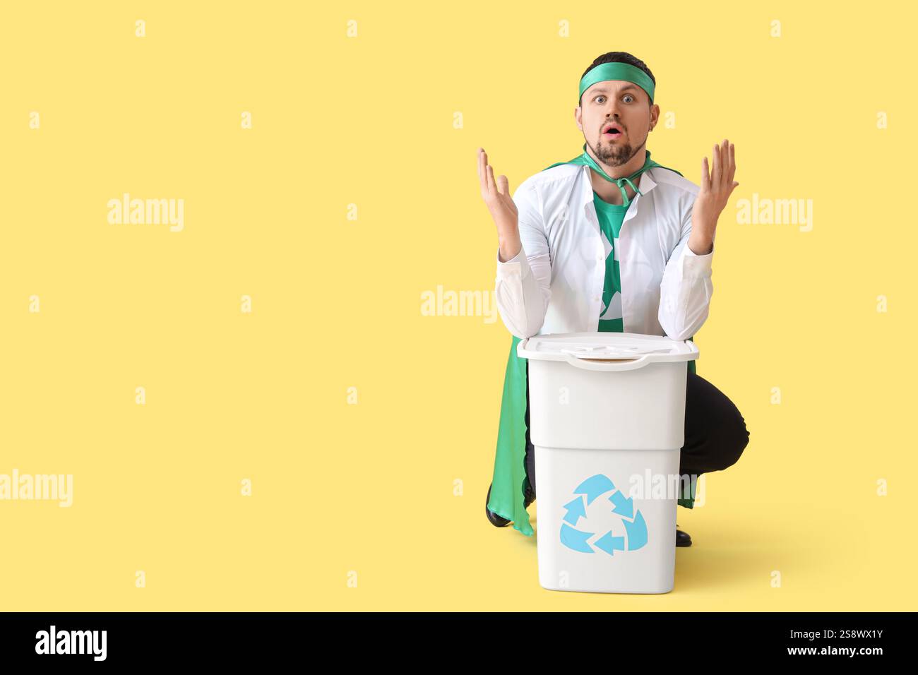 Surprised young man dressed as eco superhero with garbage bin on yellow ...