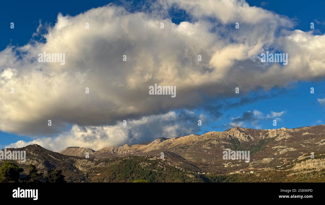 Large, billowing clouds hover above a rugged mountain range as golden ...