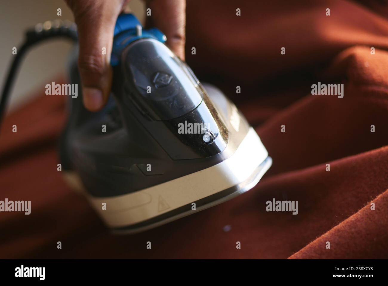 Using a steam iron to smooth out wrinkles on a brown piece of cloth ...