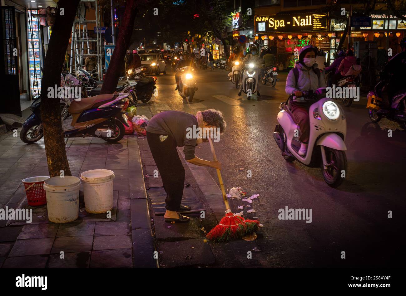 An elderly Vietnamese woman suffering from kyphosis sweeps rubbish by the side of the road in ...