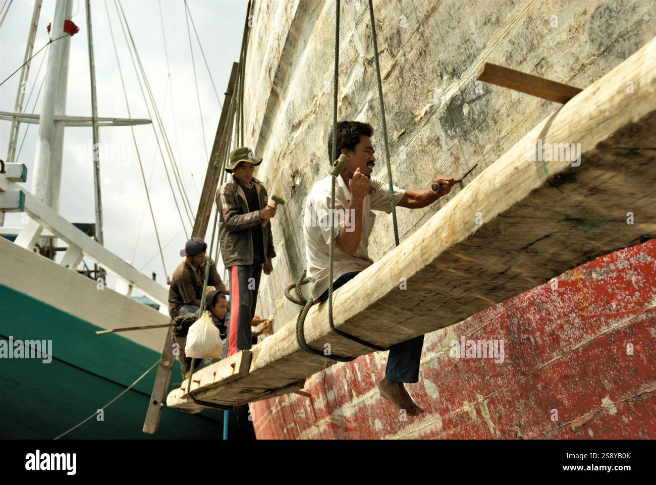 Maintenance workers repairing the hull of a phinisi ship at Sunda ...