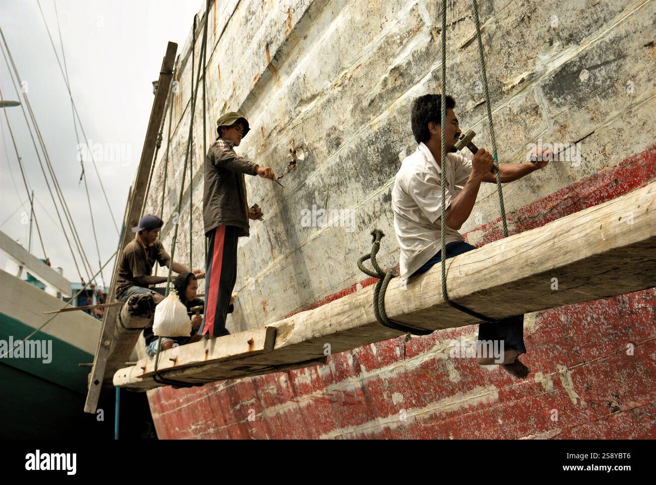 Maintenance workers repairing the hull of a phinisi ship at Sunda ...