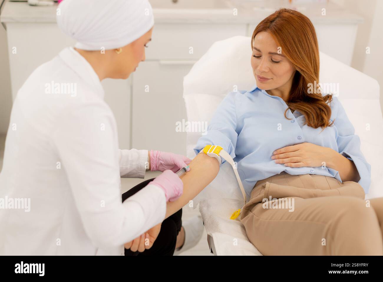 A healthcare provider gently draws blood from a patient seated ...