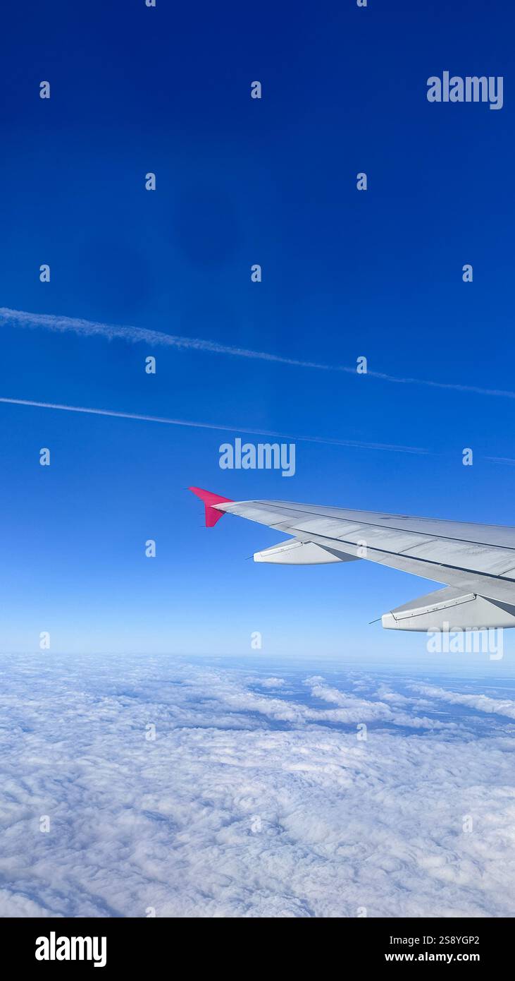 Red tail fin of an airplane is seen flying through a blue sky. The sky ...