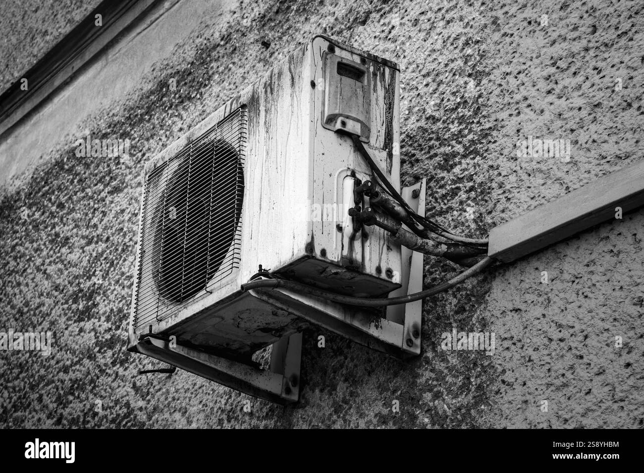 Old air conditioning unit mounted on a textured wall in black and white ...