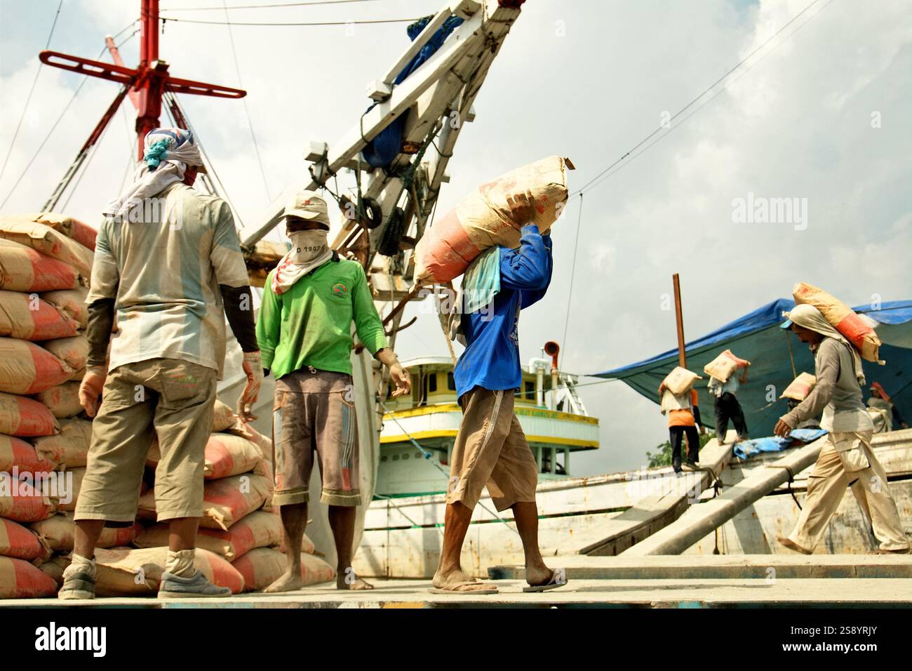 Workers transporting cement sacks from a truck onto a phinisi ship at ...