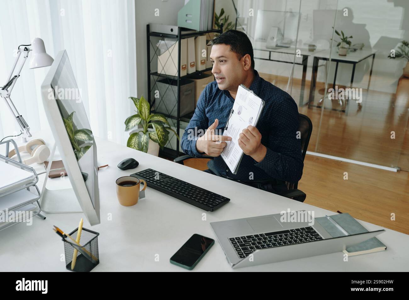 Man in office holding tablet while speaking during a video call ...