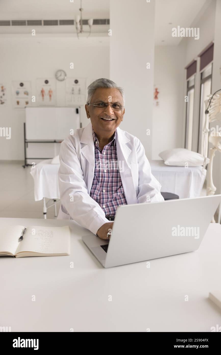 Portrait happy smiling older age doctor sitting at office workplace ...