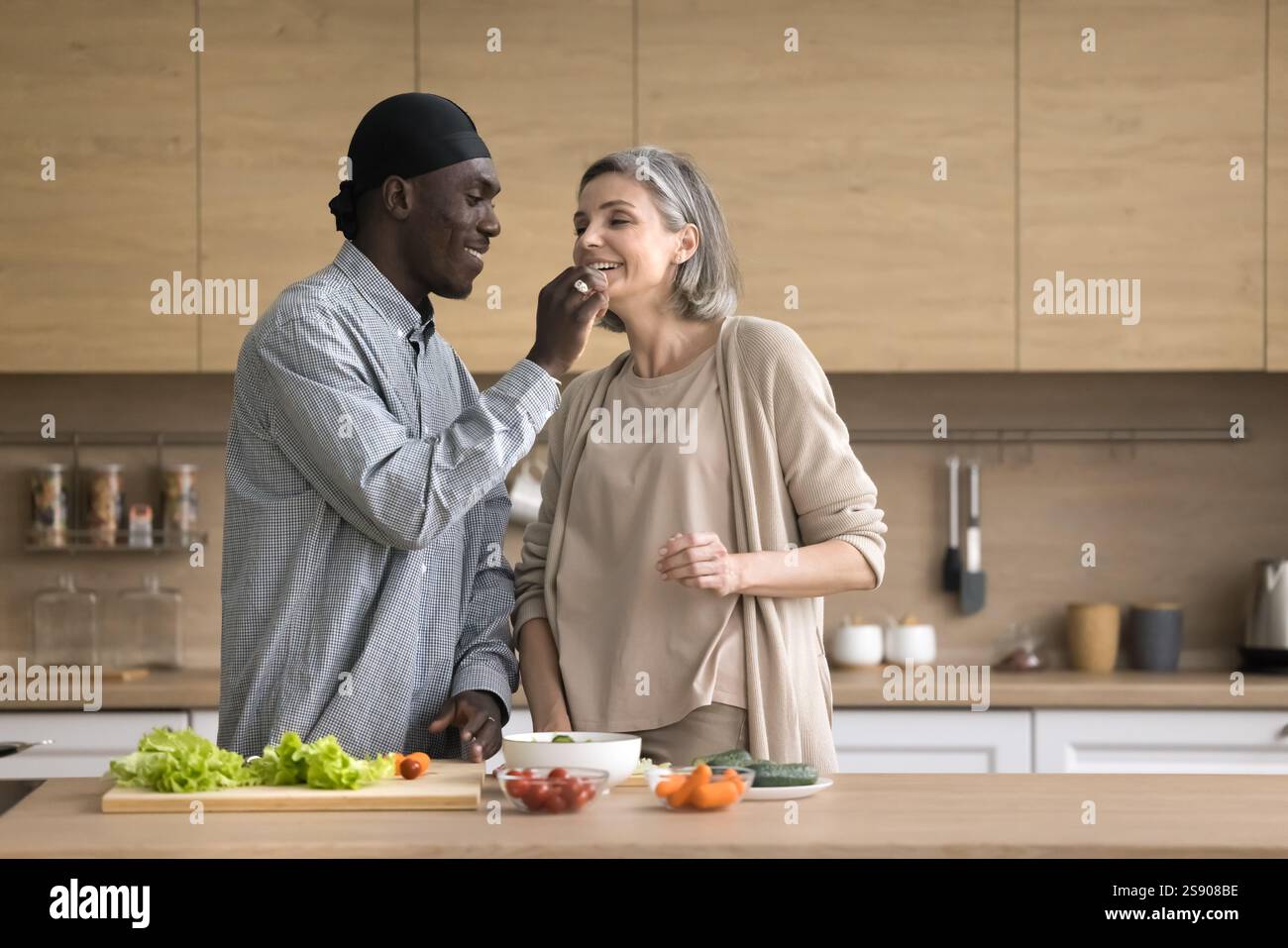 Affectionate loving African husband cook food with mature European wife ...