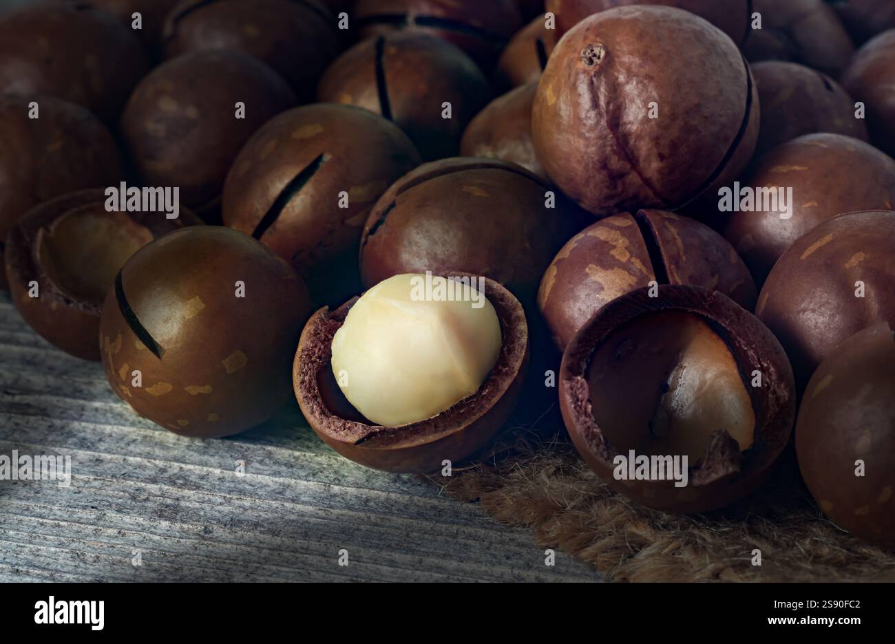 Macadamia nuts in cracked shells are arranged neatly on a rustic wooden ...