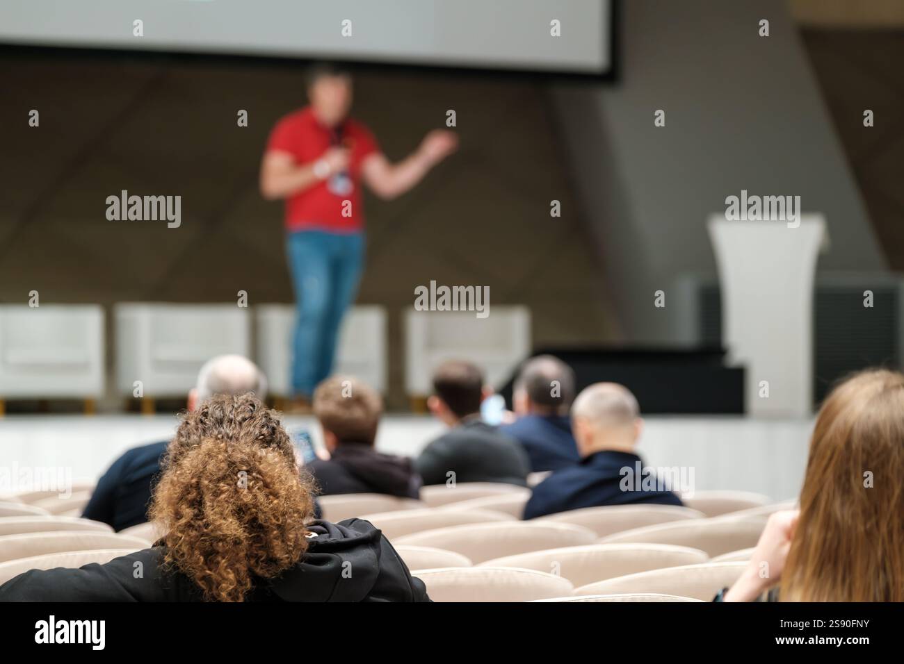 Conference audience listening to energetic speaker in modern auditorium ...