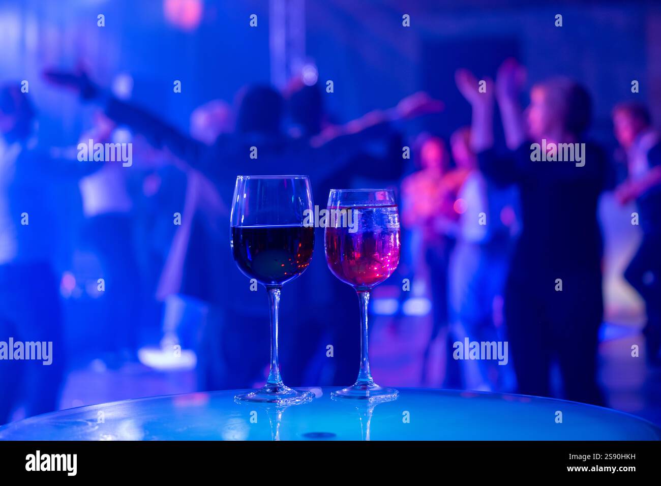 Two wine glasses on table amidst lively party atmosphere with people ...