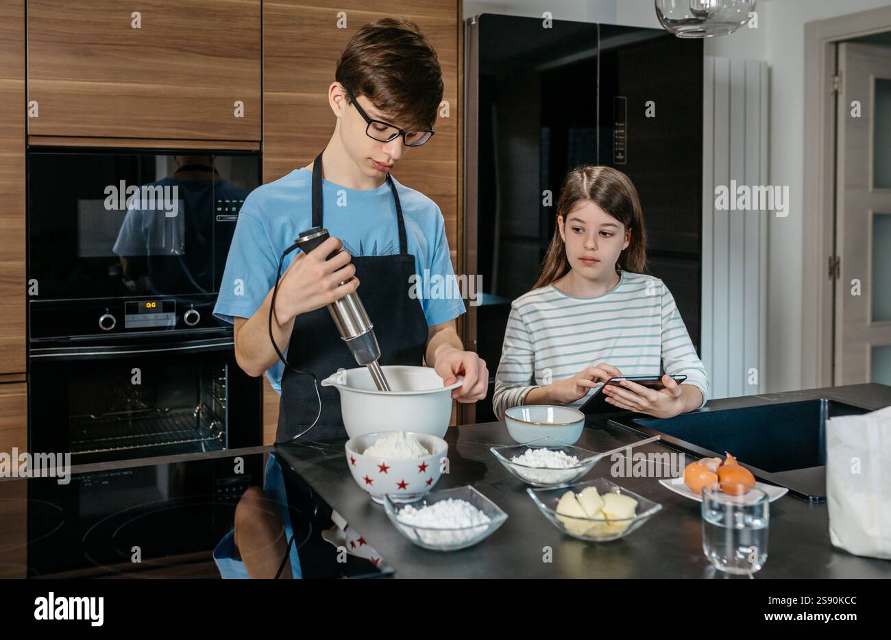 Brother and sister cooking together while following recipe on tablet ...