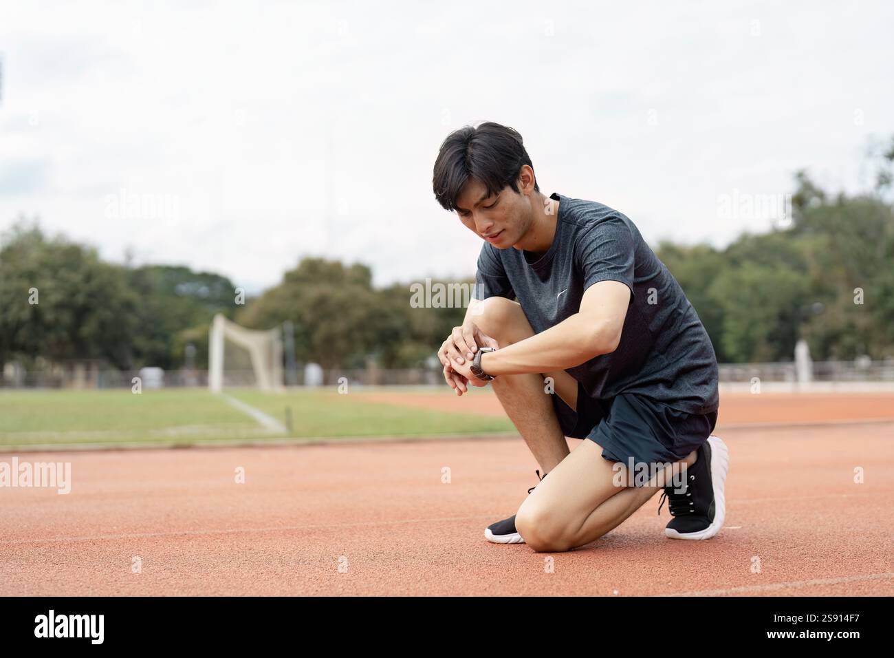 Focused young man monitoring fitness progress while resting on a track ...