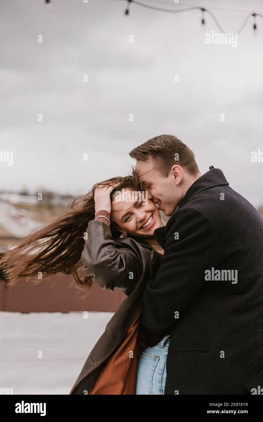 Fun couple embracing on a rooftop, hair blowing in the wind Stock Photo ...