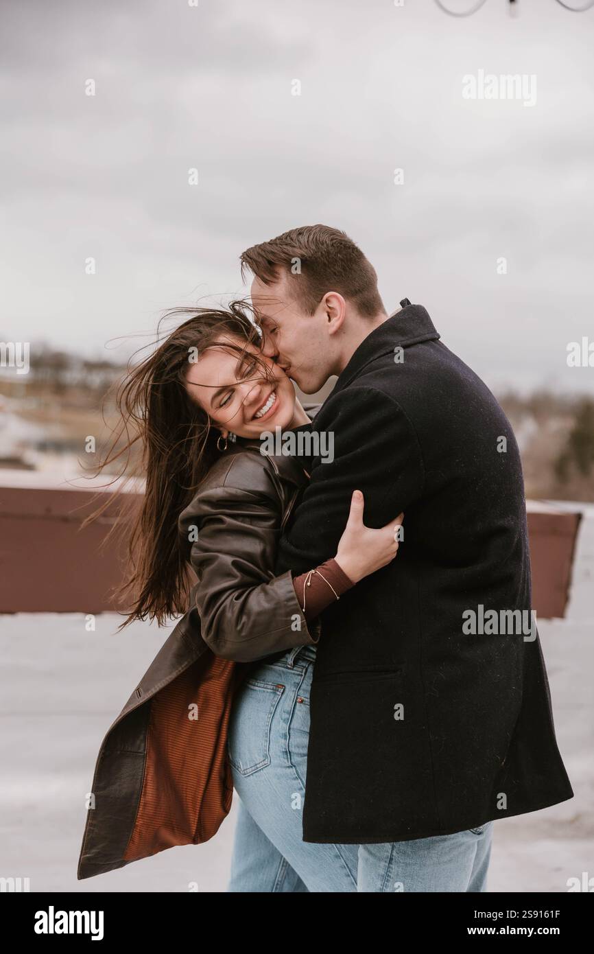 Fun couple embracing on a rooftop, hair blowing in the wind Stock Photo ...