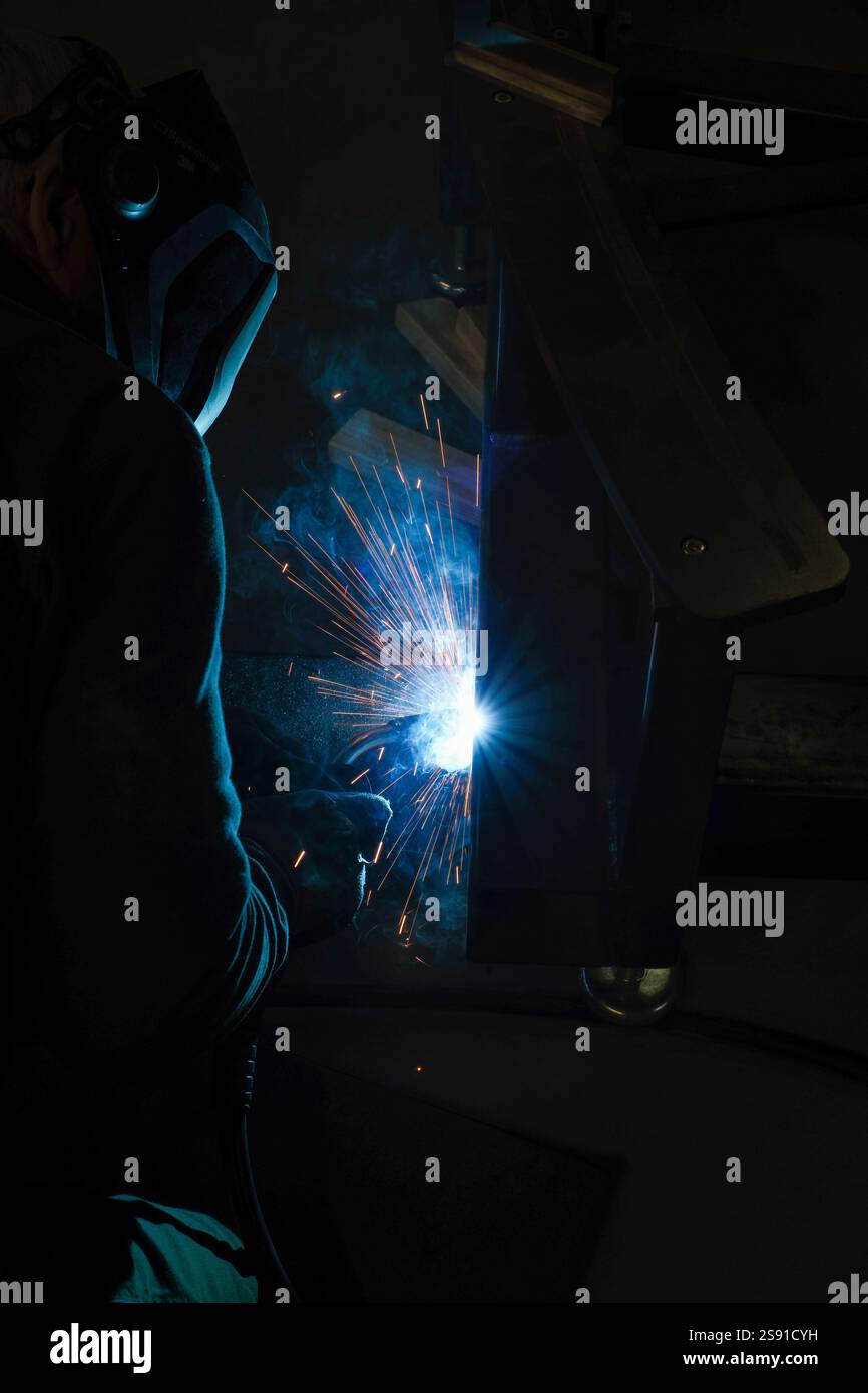 A person wearing a welding mask works on metal with a welding torch ...