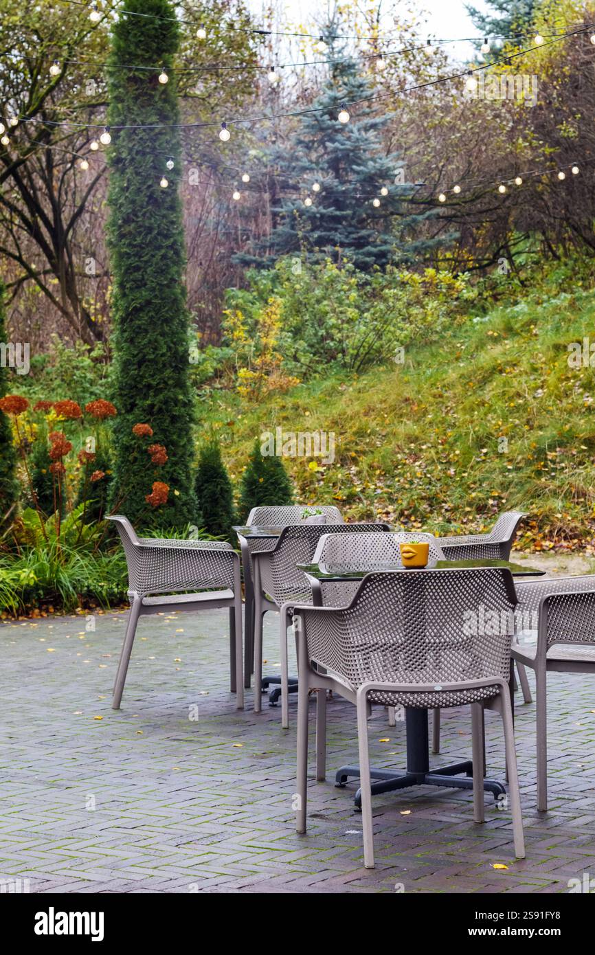 An empty cafe square with a few tables and chairs set in a green park ...