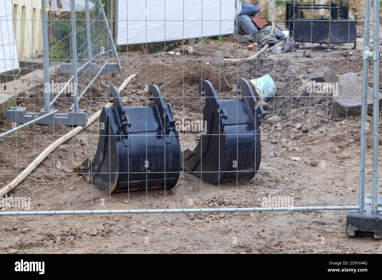 Two excavator buckets placed in a construction pit surrounded by a ...