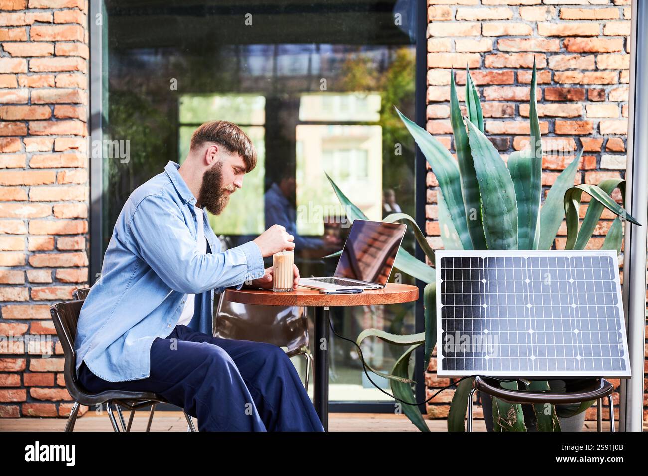 Man works on laptop at outdoor round table, with glass of iced coffee ...