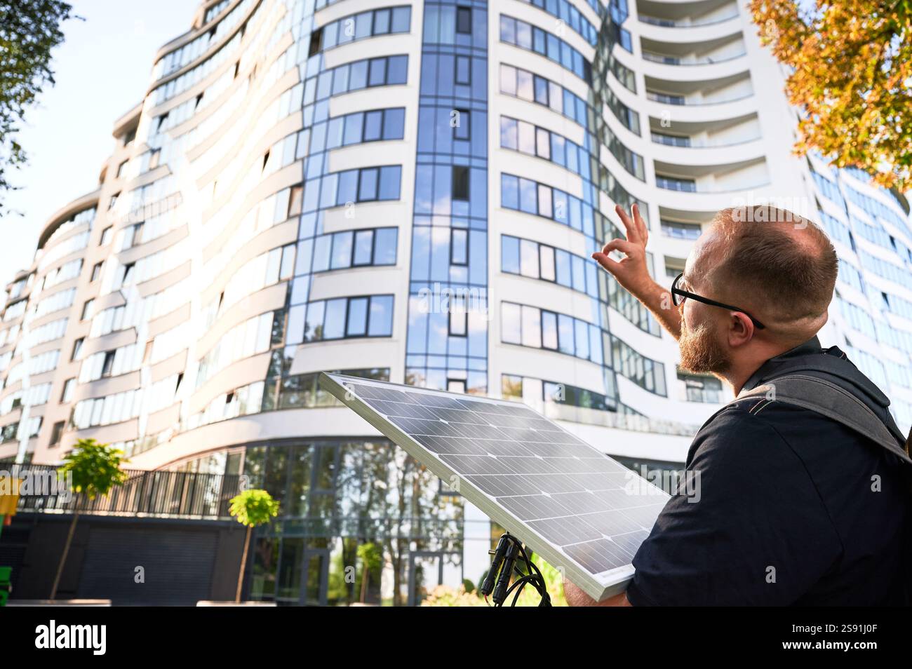 Man holding photovoltaic solar panel in front of new building, showing ...