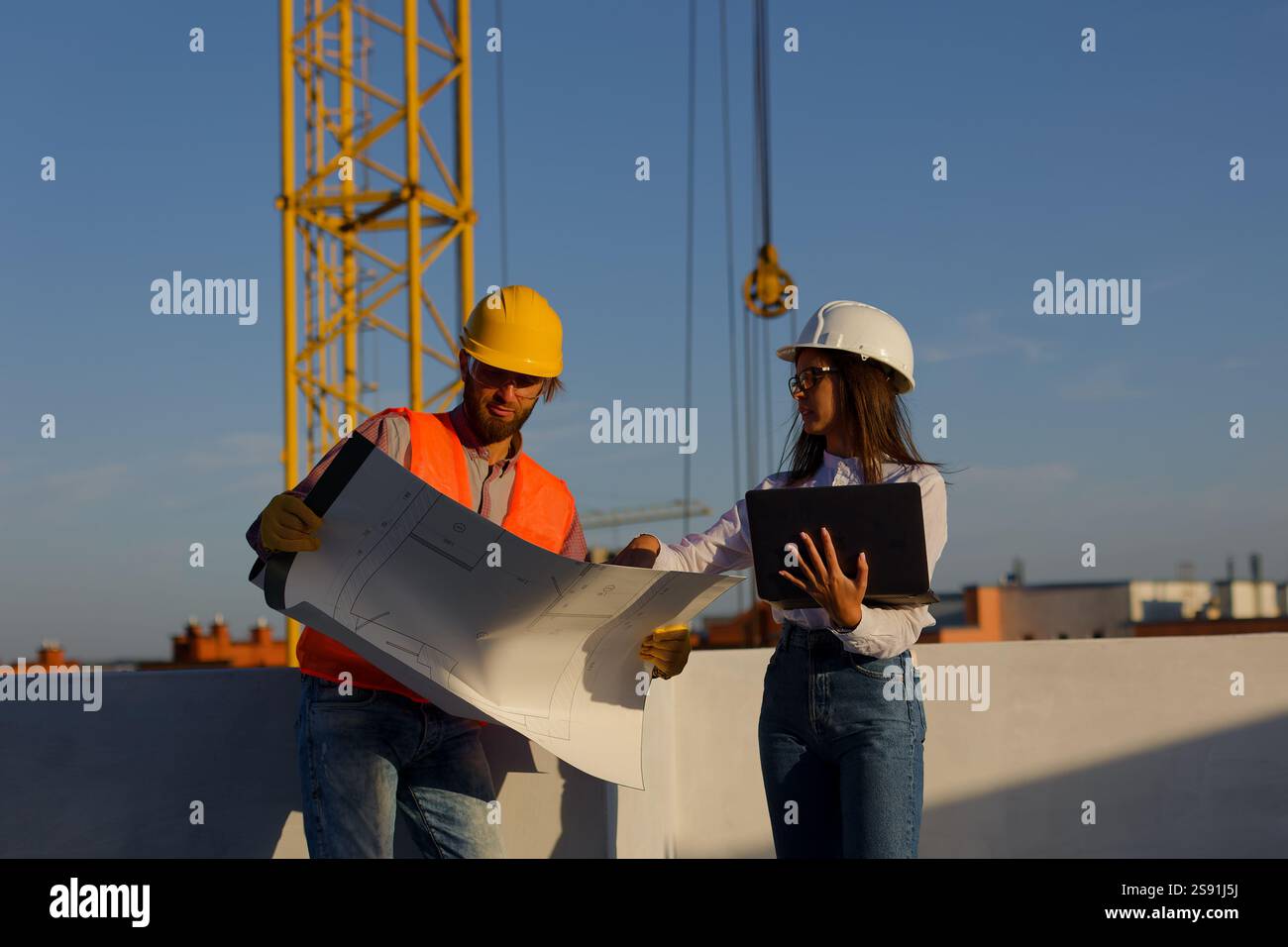 Construction workers reviewing blueprints on a building site with crane ...